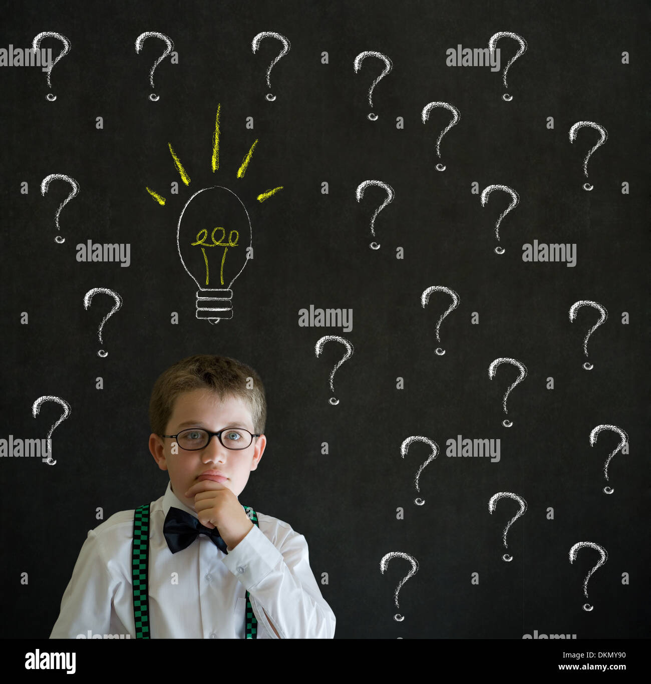 Thinking boy dressed up as business man questioning ideas on blackboard ...