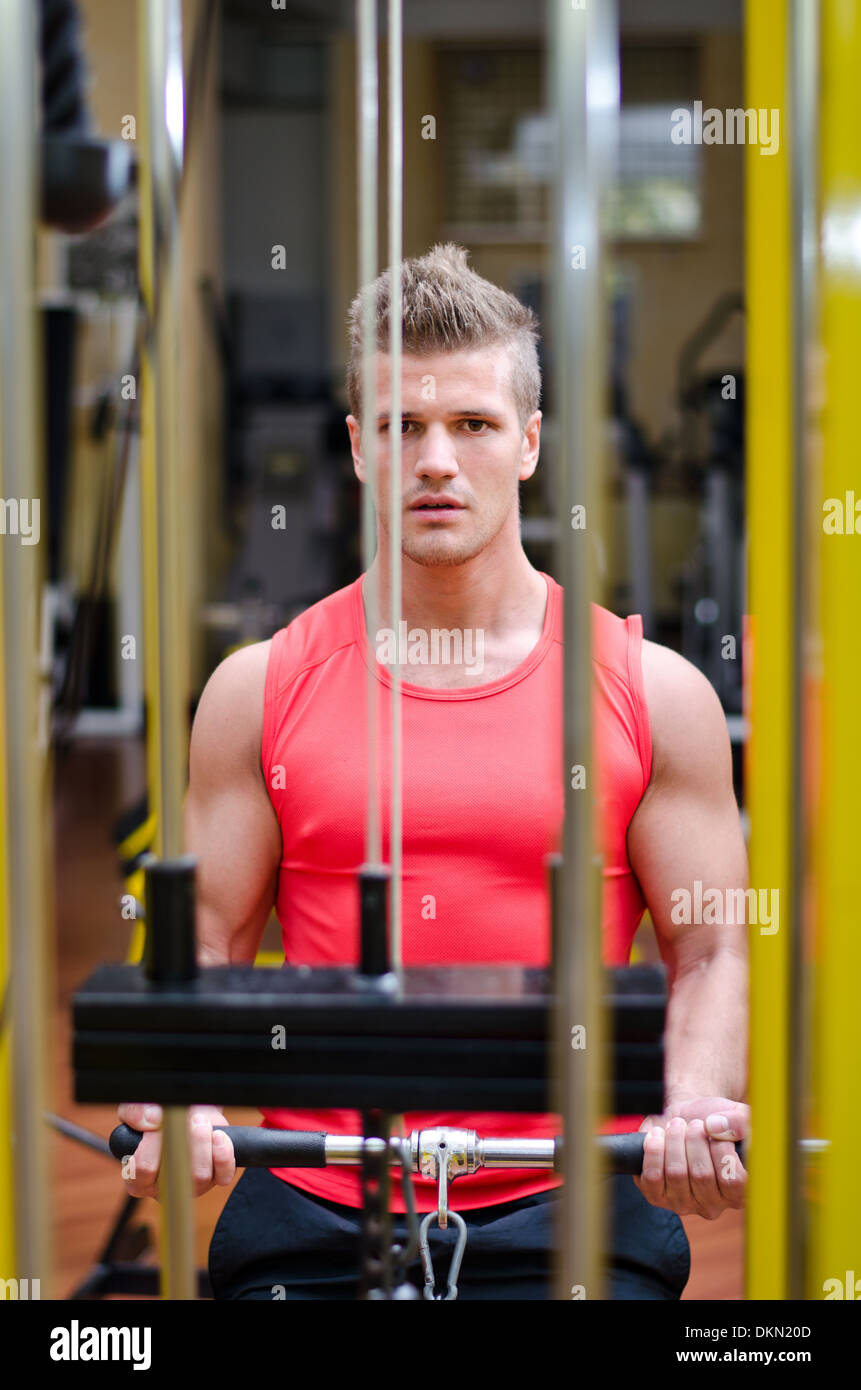 Handsome young man in gym working out, exercising biceps on equipment ...