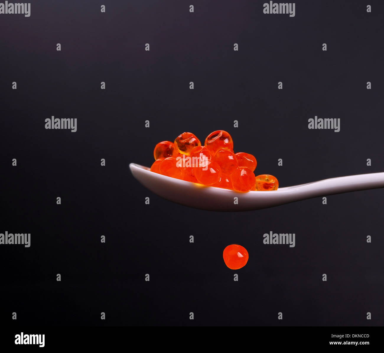 Porcelain spoon full of flying red caviar on black background, close up ...