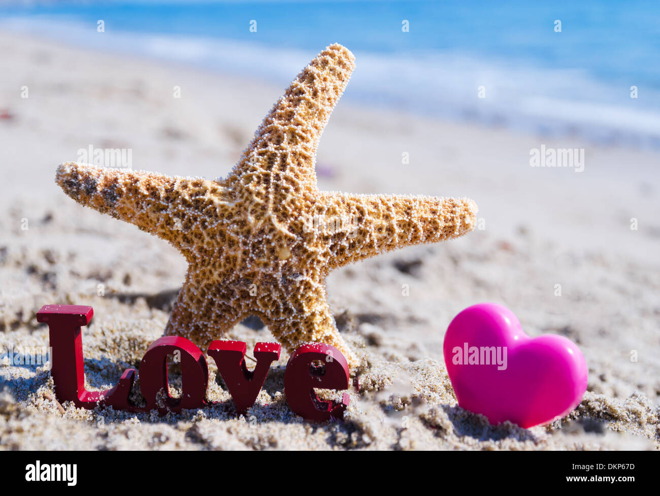 Sign "LOVE" with starfish and heart on the sandy beach by the ocean ...