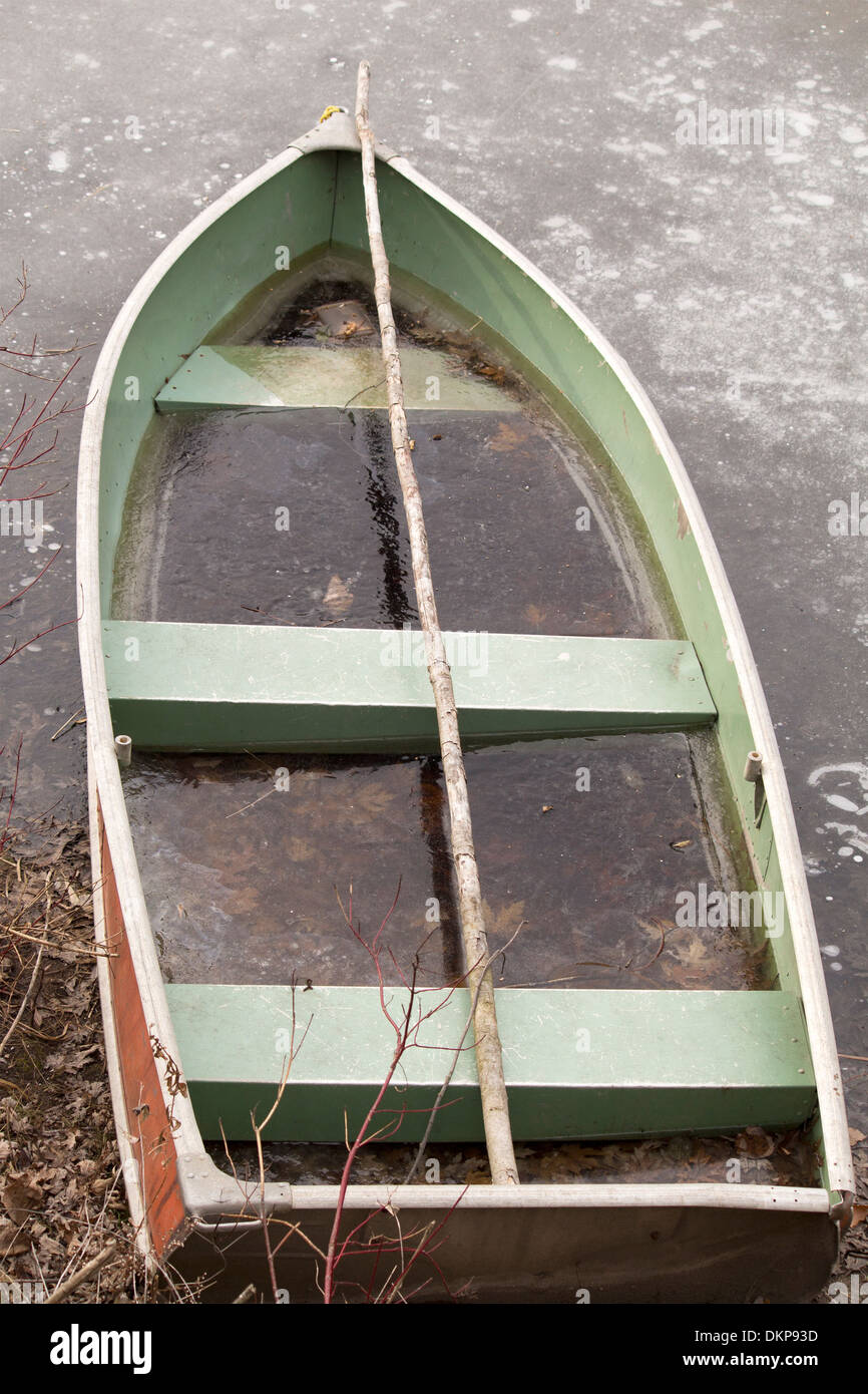 Rowboat on bank slightly sunk in icy water with water and ice inside ...