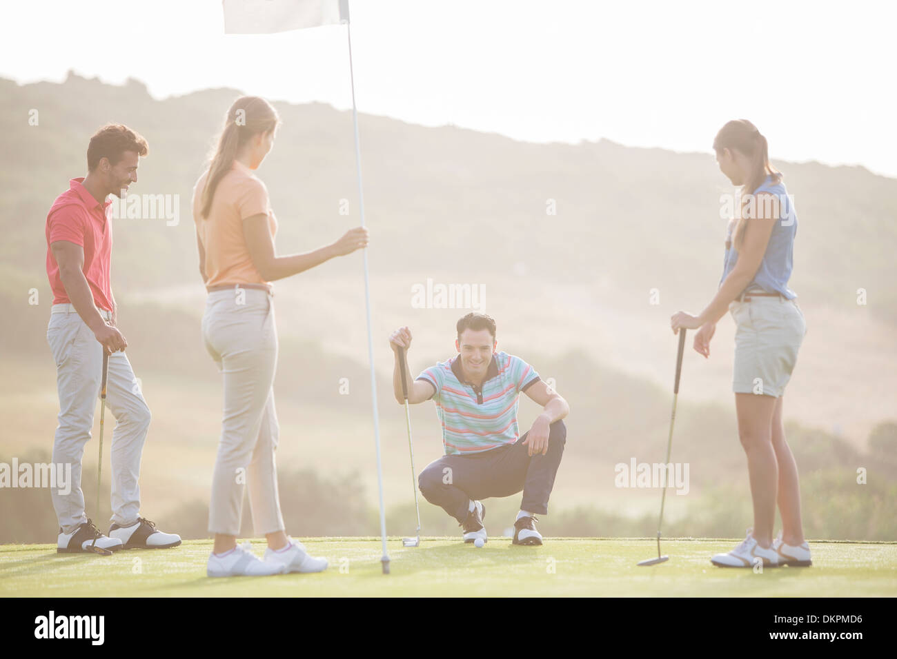 Friends watching man prepare to putt on golf course Stock Photo - Alamy