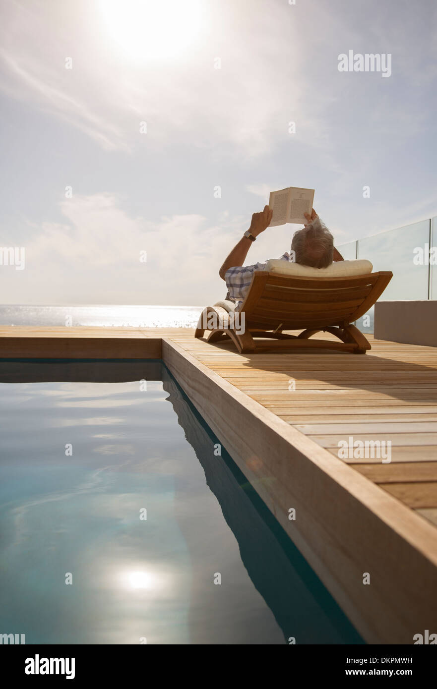 Man reading in lawn chair by pool Stock Photo - Alamy