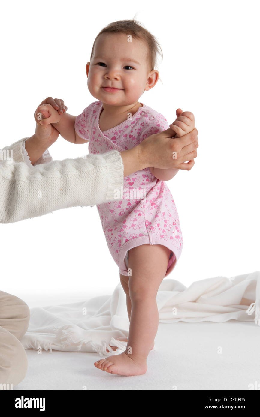 Toddler girl standing with help of mothers hands on white background ...