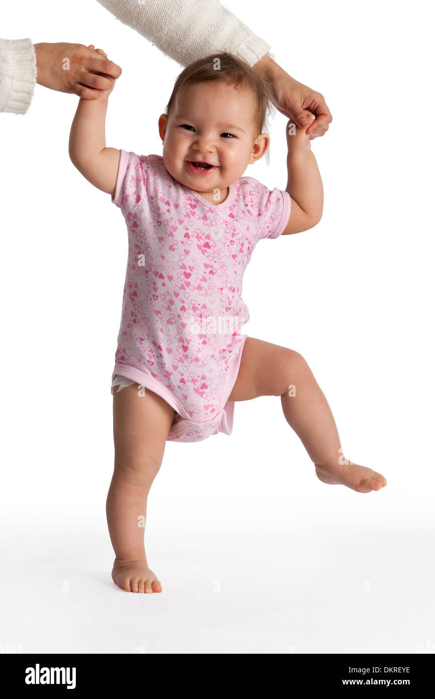 Toddler girl walking with help of mothers hands on white background ...