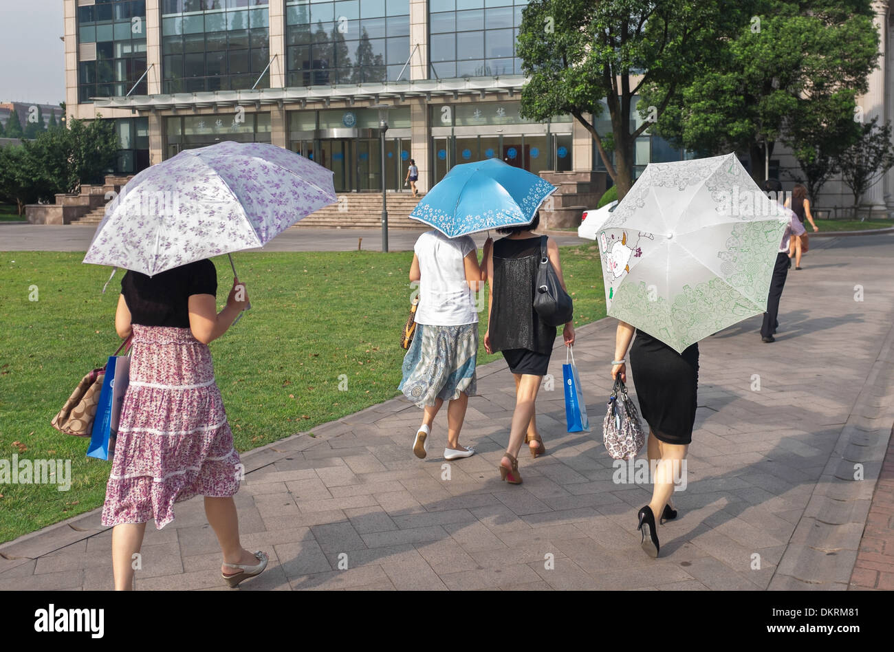 Women walking with umbrellas to shade from sun on campus of Fudan ...