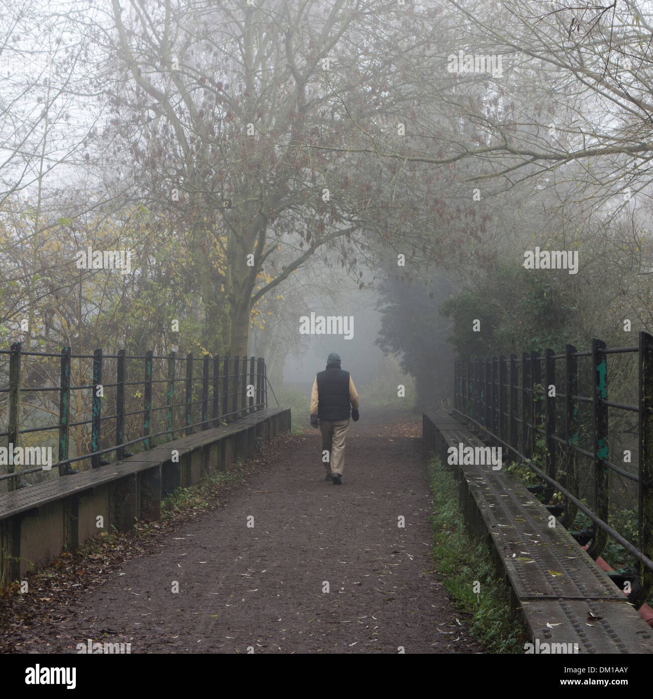 Winter walk: a solitary man walks along a bridge, into mist, on a ...