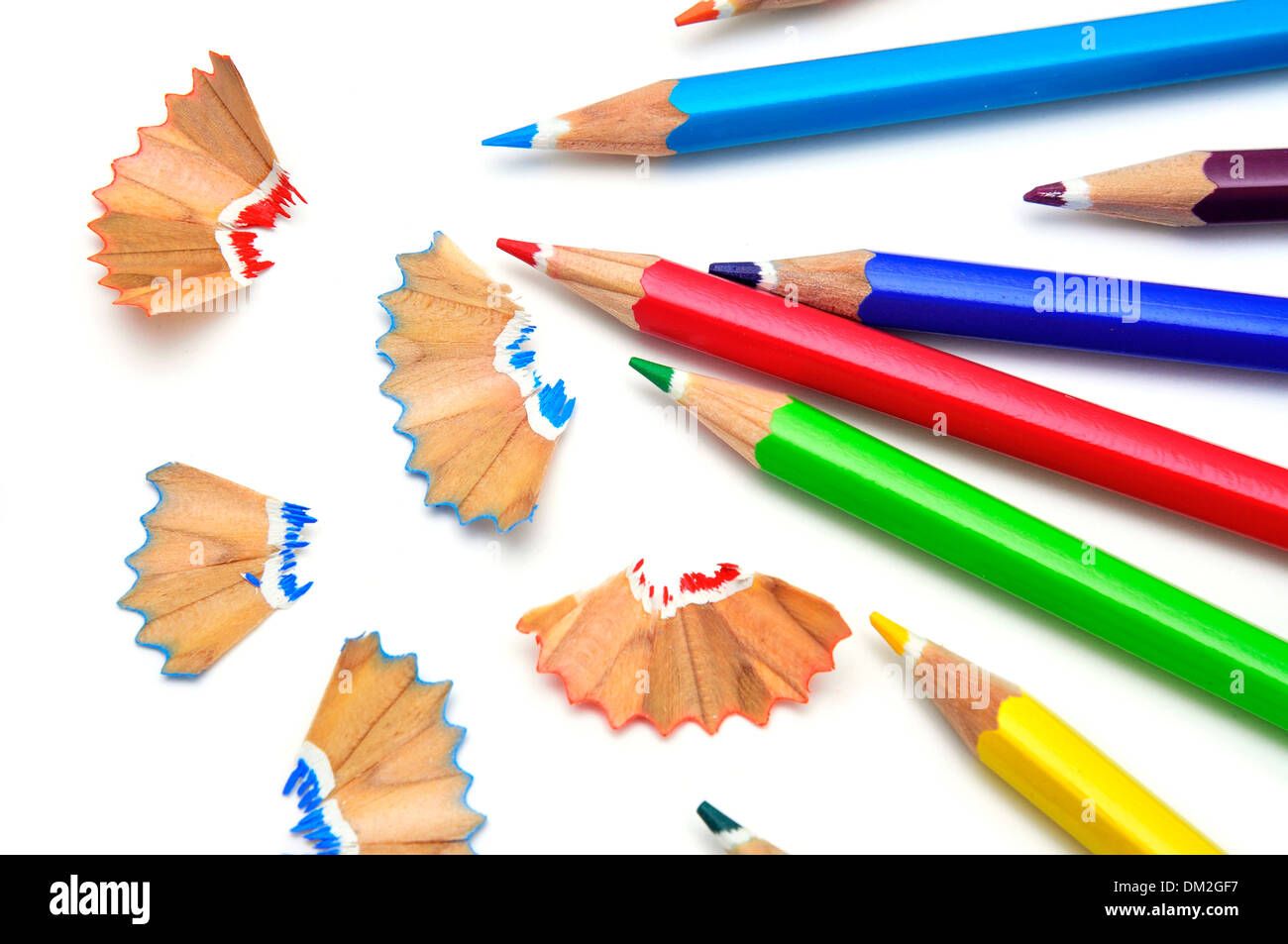 some colored pencils of different colors and pencil shavings on a white ...