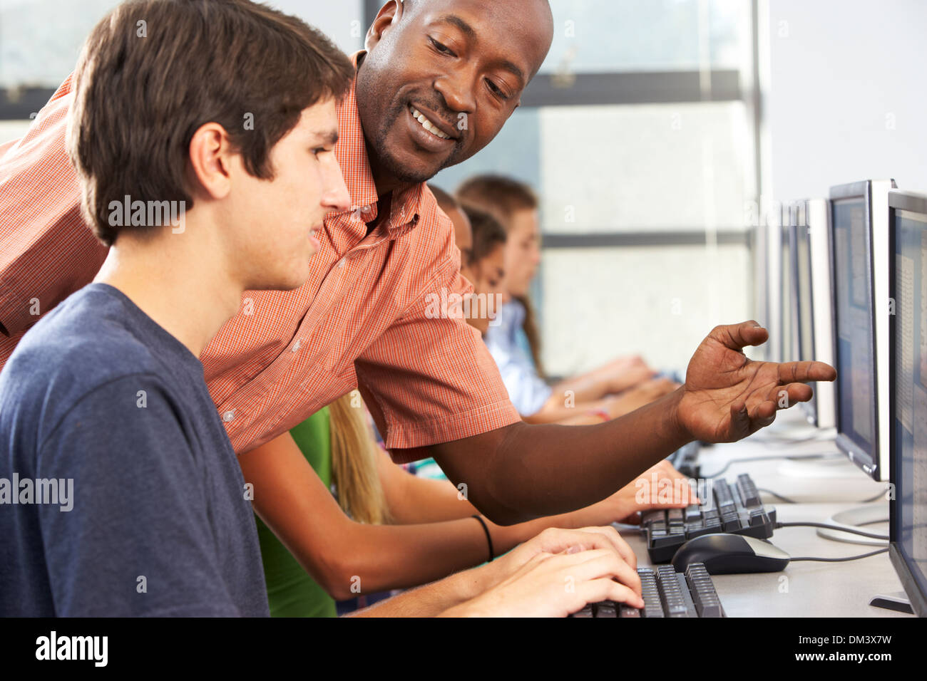 Teacher Helping Students Working At Computers In Classroom Stock Photo ...