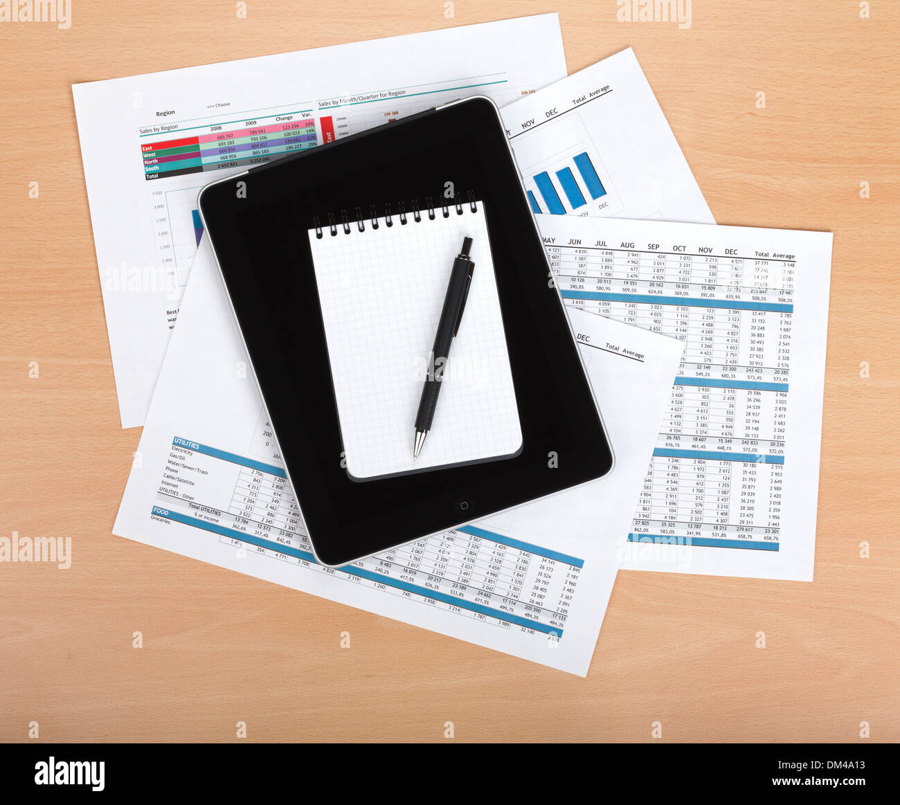 Tablet and notepad over papers with numbers and charts, coffee cup ...