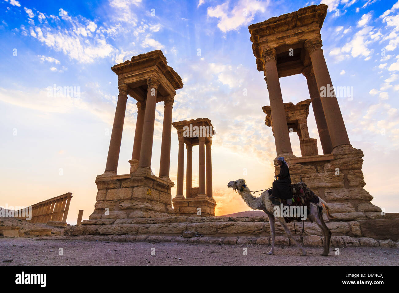 Man on camel at sunset beside the Tetrapylon of the ruins at Palmyra ...