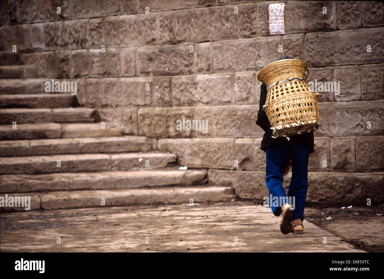 A porter carrying a wicker basket on his back, he is transporting goods ...
