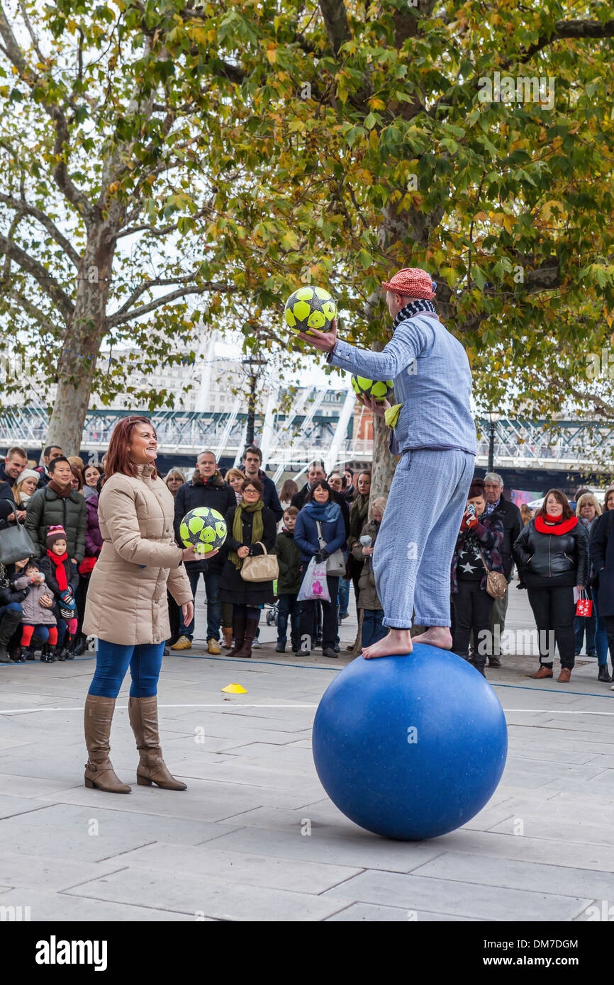 Street Performer juggler on blue ball juggles balls with help from ...