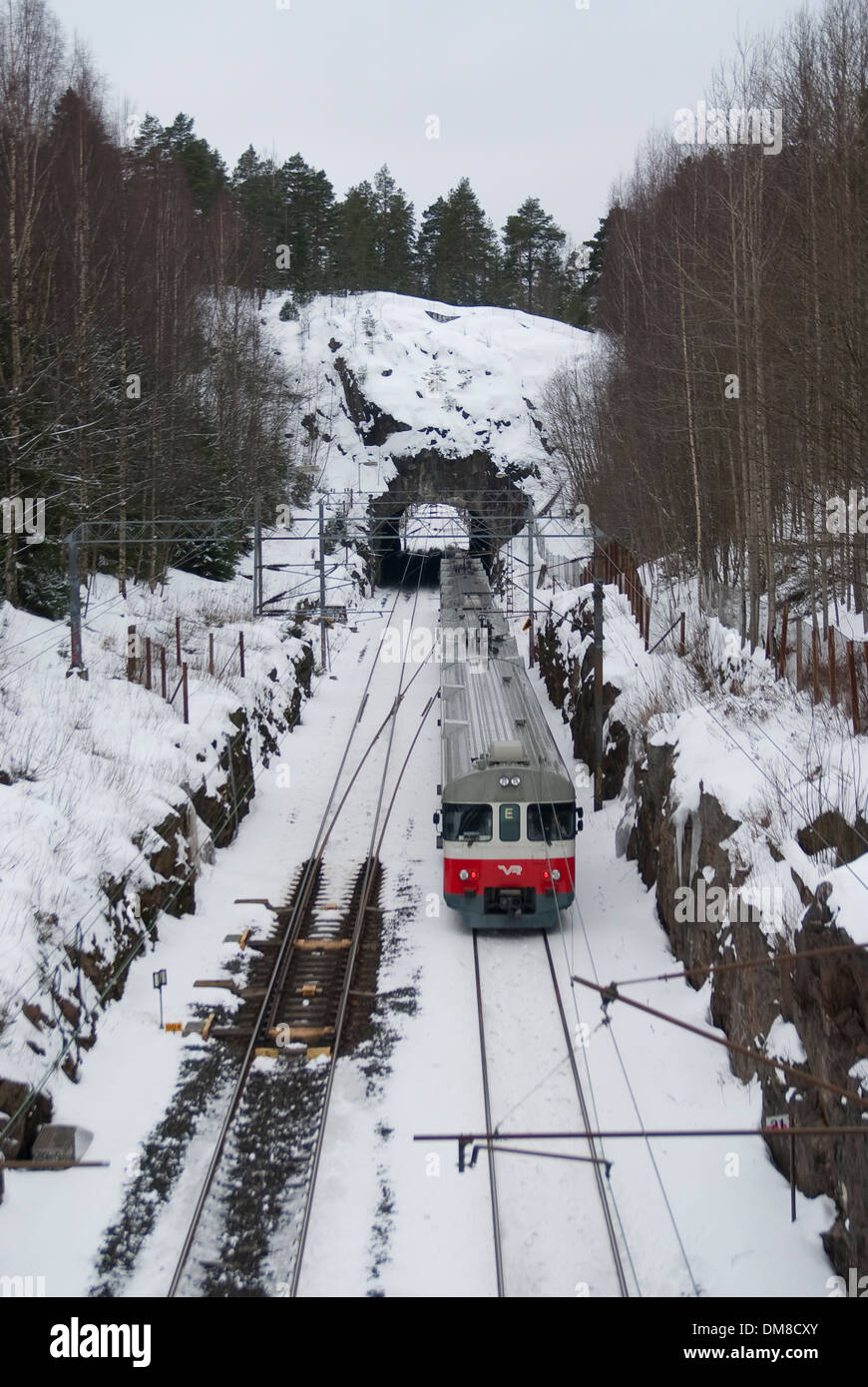 Train heading for a short tunnel under a big rock formation on a snowy ...