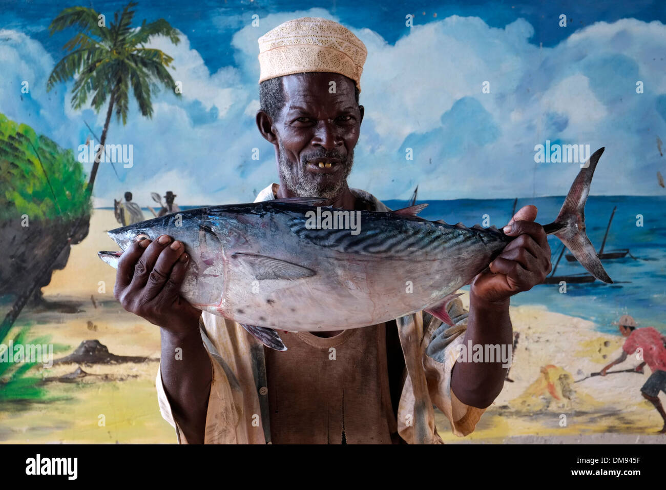 A fishmonger holds a Tuna fish as he stands next to a painted wall in ...