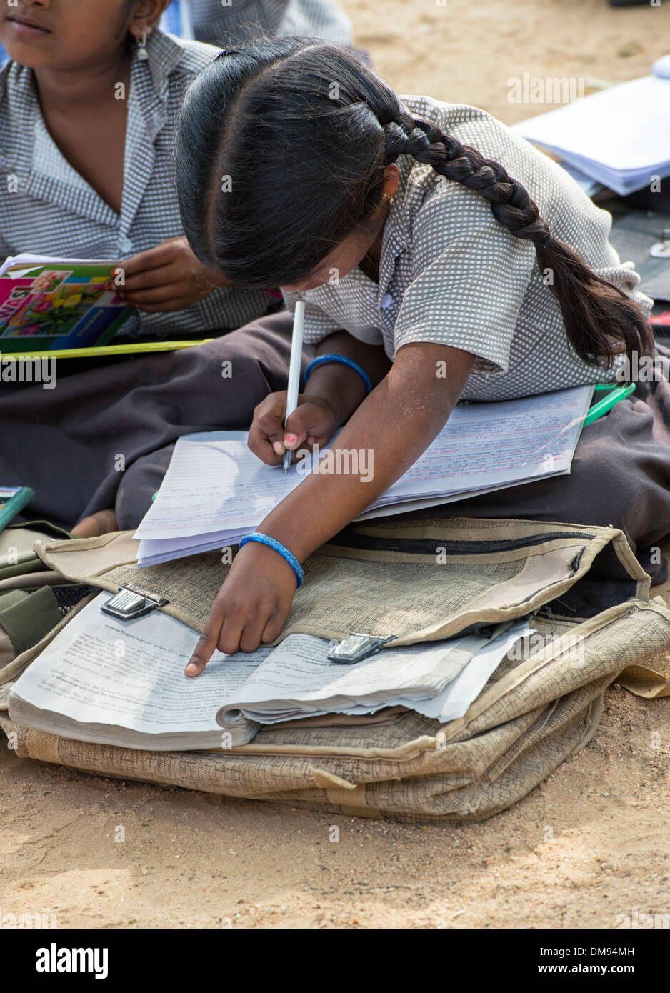 Rural Indian village school girl writing in a textbook in an outside ...
