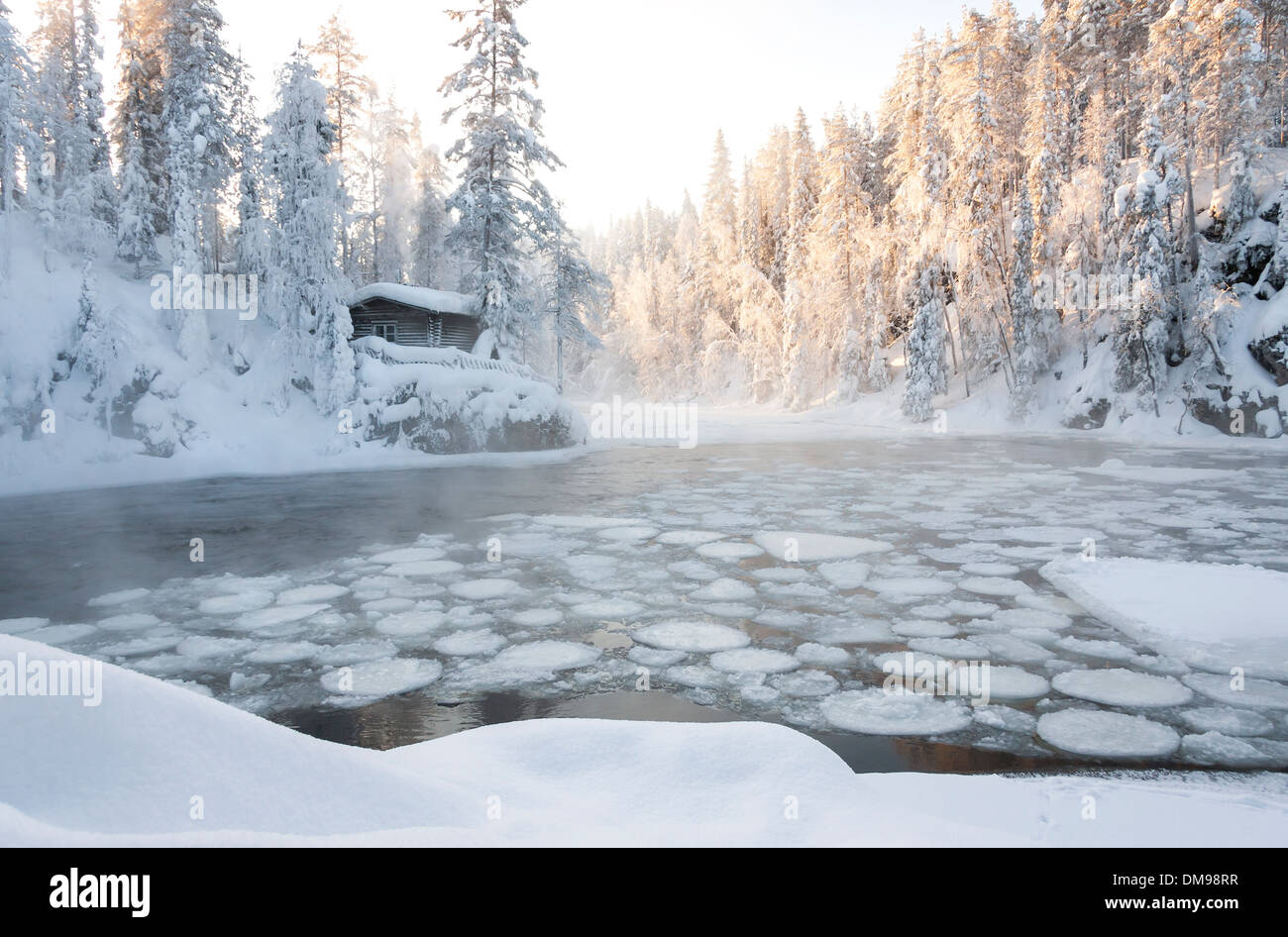 Small hut or log cabin at the cliff edge near icy pond in white snowy ...