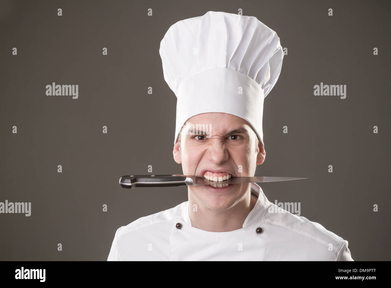 Portrait of smiling chef with knife in mouth isolated on grey ...