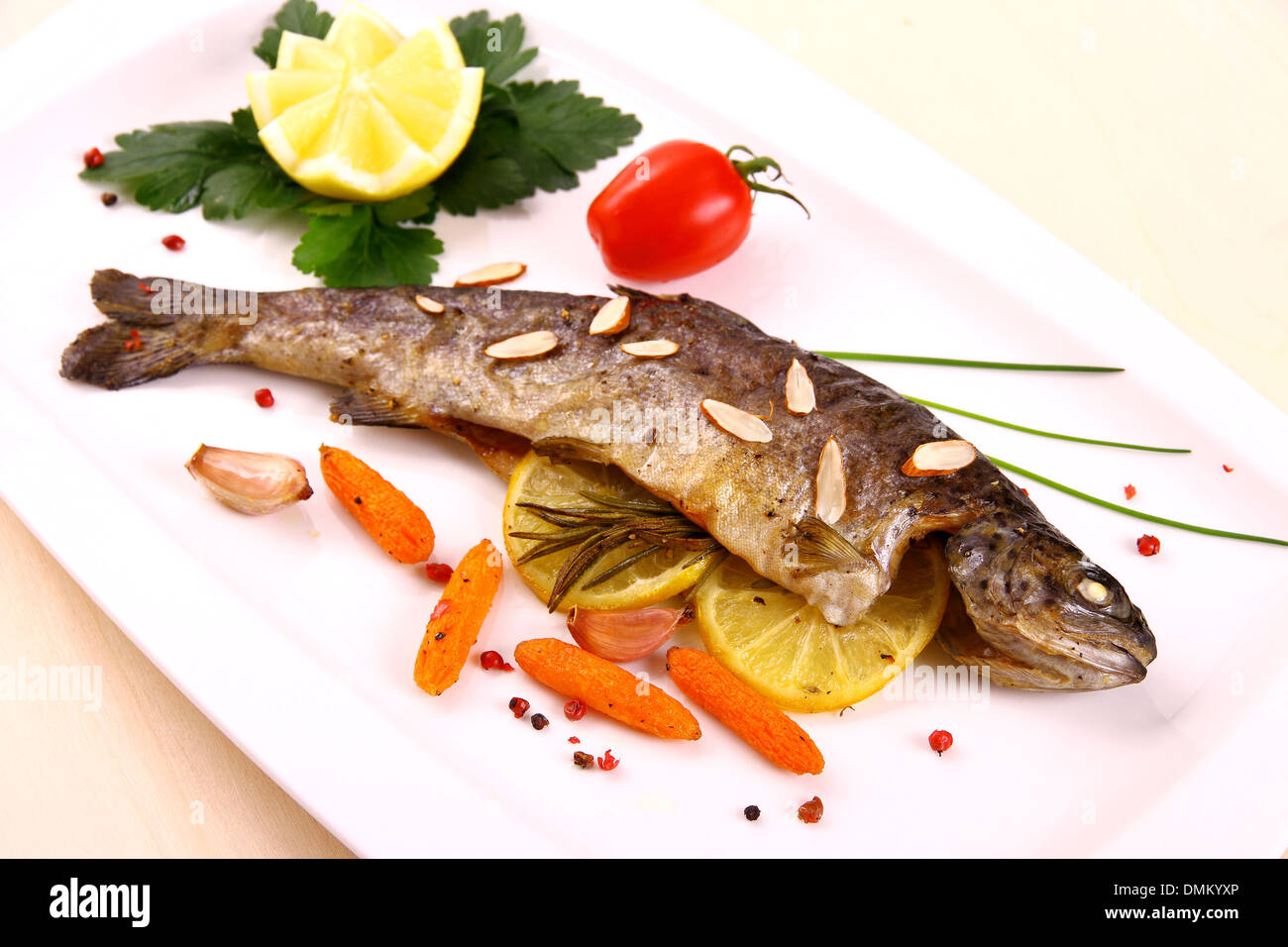 Fried trout with vegetables and split almonds on white plate ...