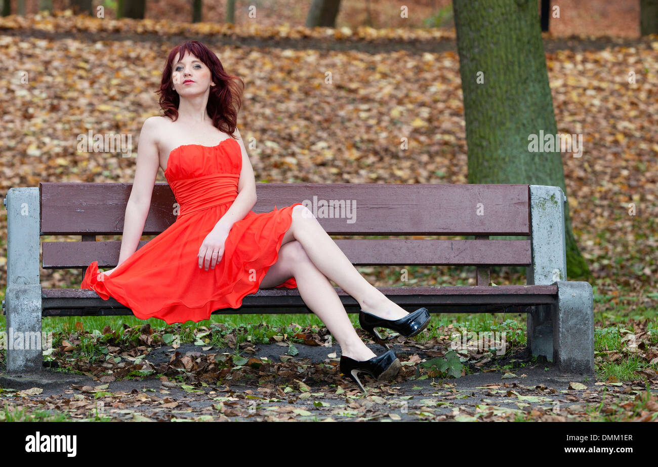 Beautiful young woman in elegant red dress sitting on bench. Girl ...