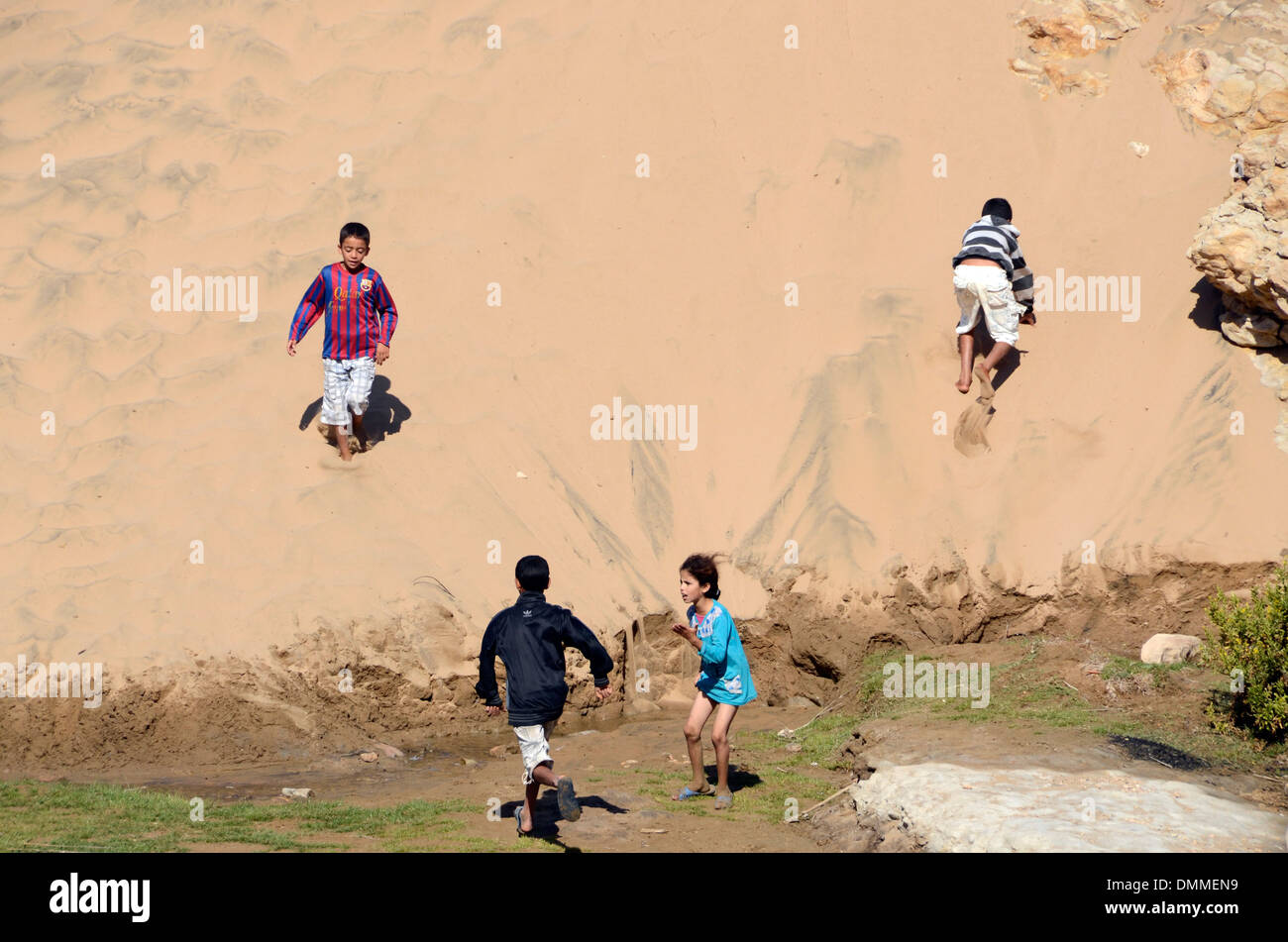 Berber children playing on sand dunes at an oasis near their village ...