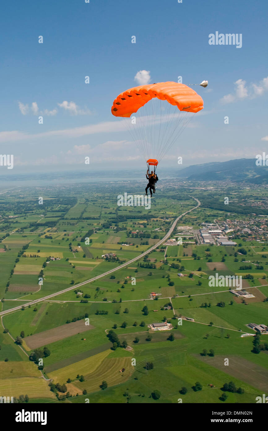 Two skydivers under a tandem canopy are flying over a spectacular land ...