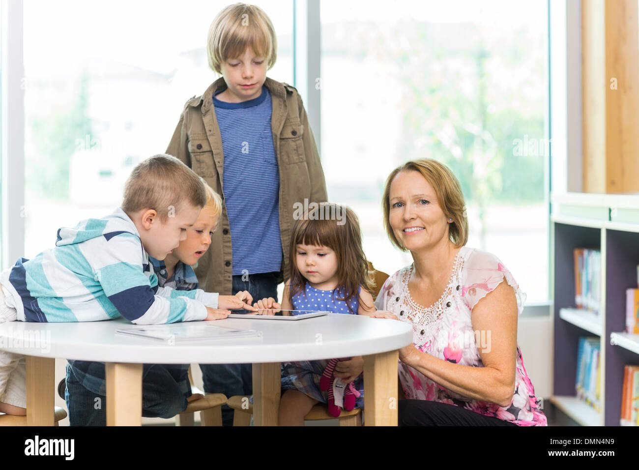 Teacher With Students Using Tablet Computer In Library Stock Photo - Alamy
