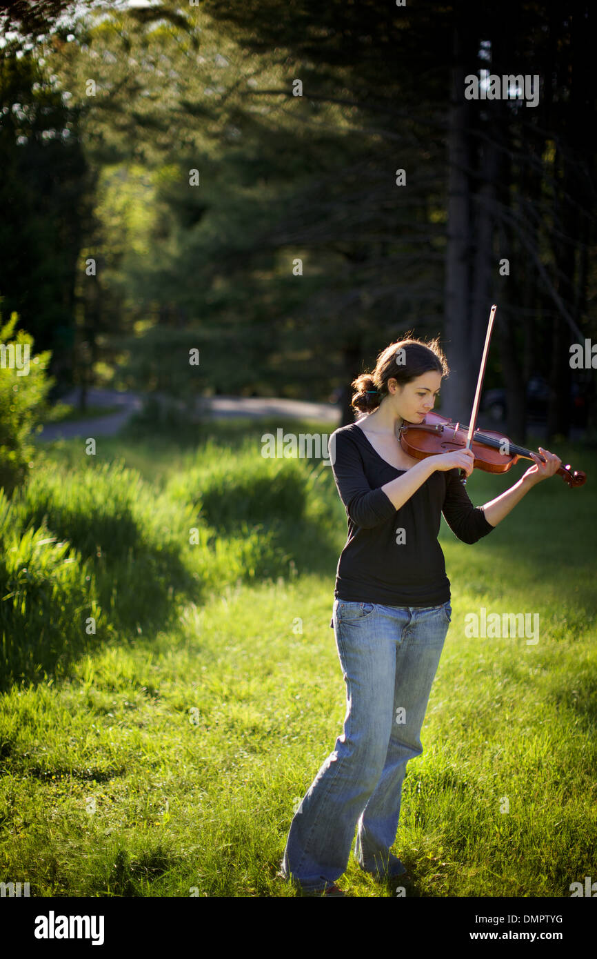 Cute young brunette girl in jeans saws on her fiddle, illuminated from ...