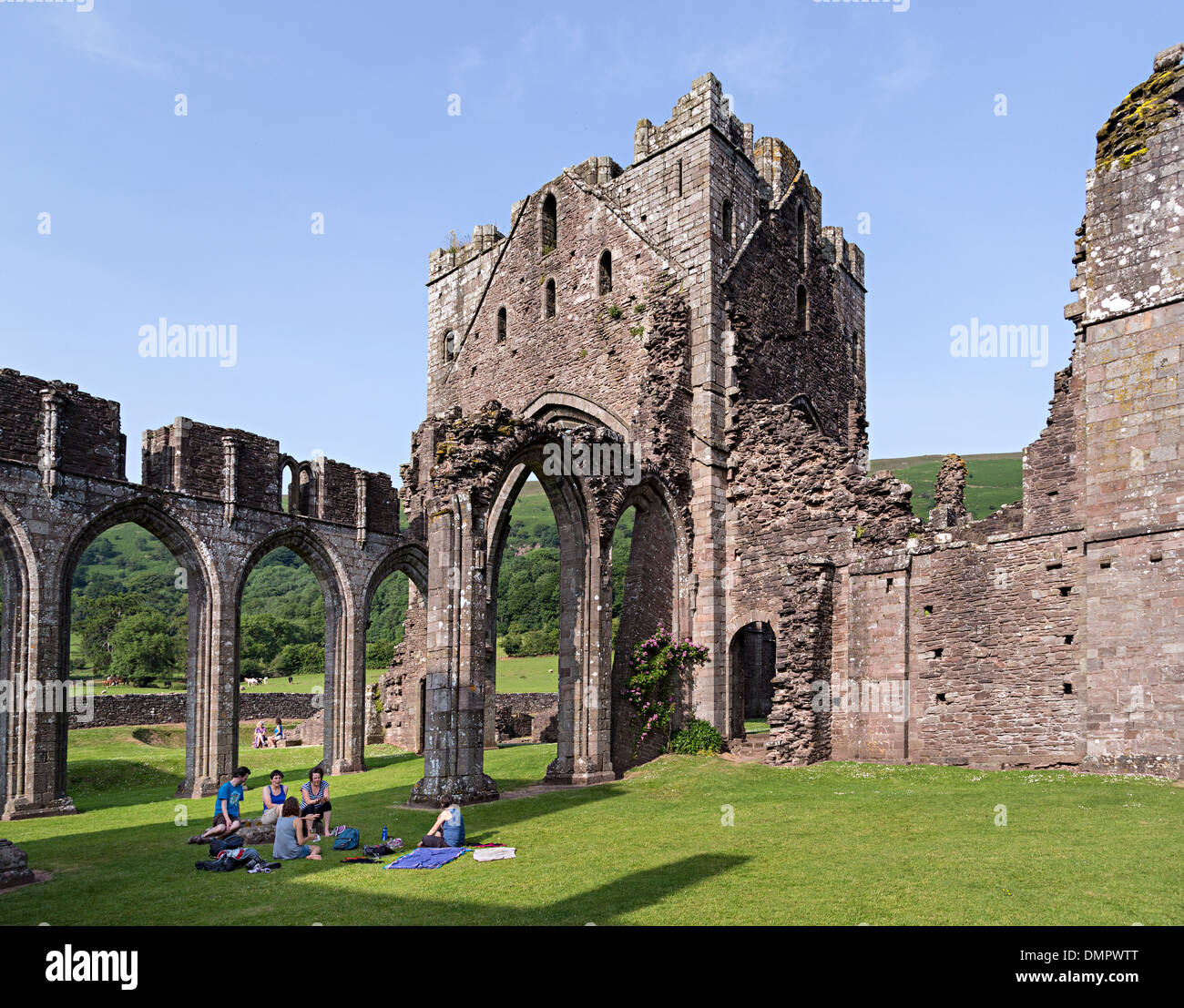 People sitting on grass in sunshine at Llantony Priory ruins, Vale of ...