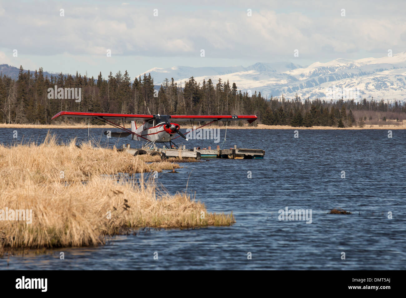 Red floatplane on an Alaskan lake in fall with snow covered mountains ...
