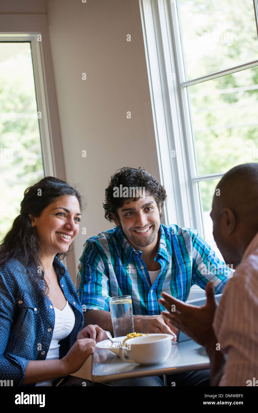 Three people seated at a cafe table talking Stock Photo - Alamy