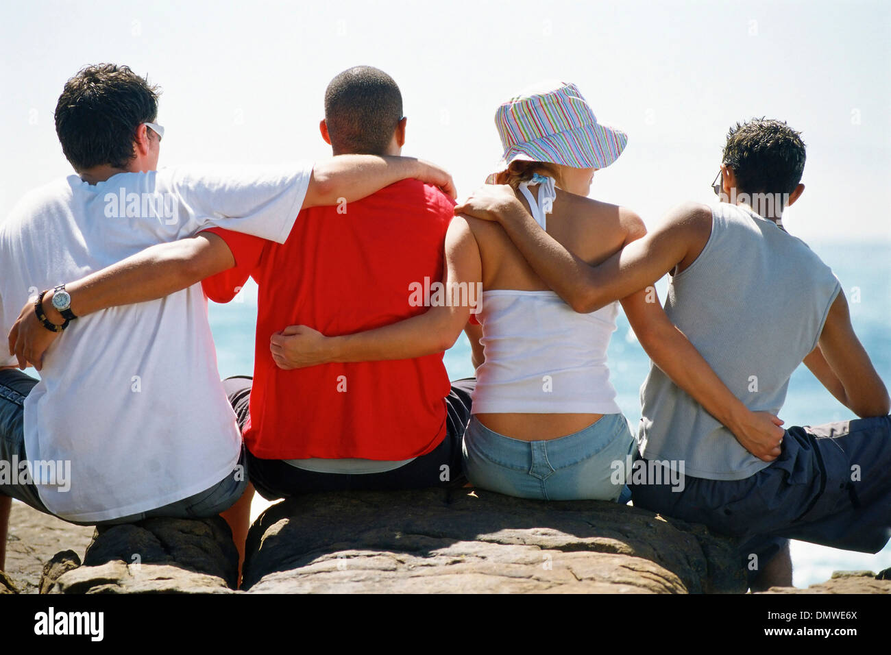 Back view of four friends with arms around each or sitting in a row ...