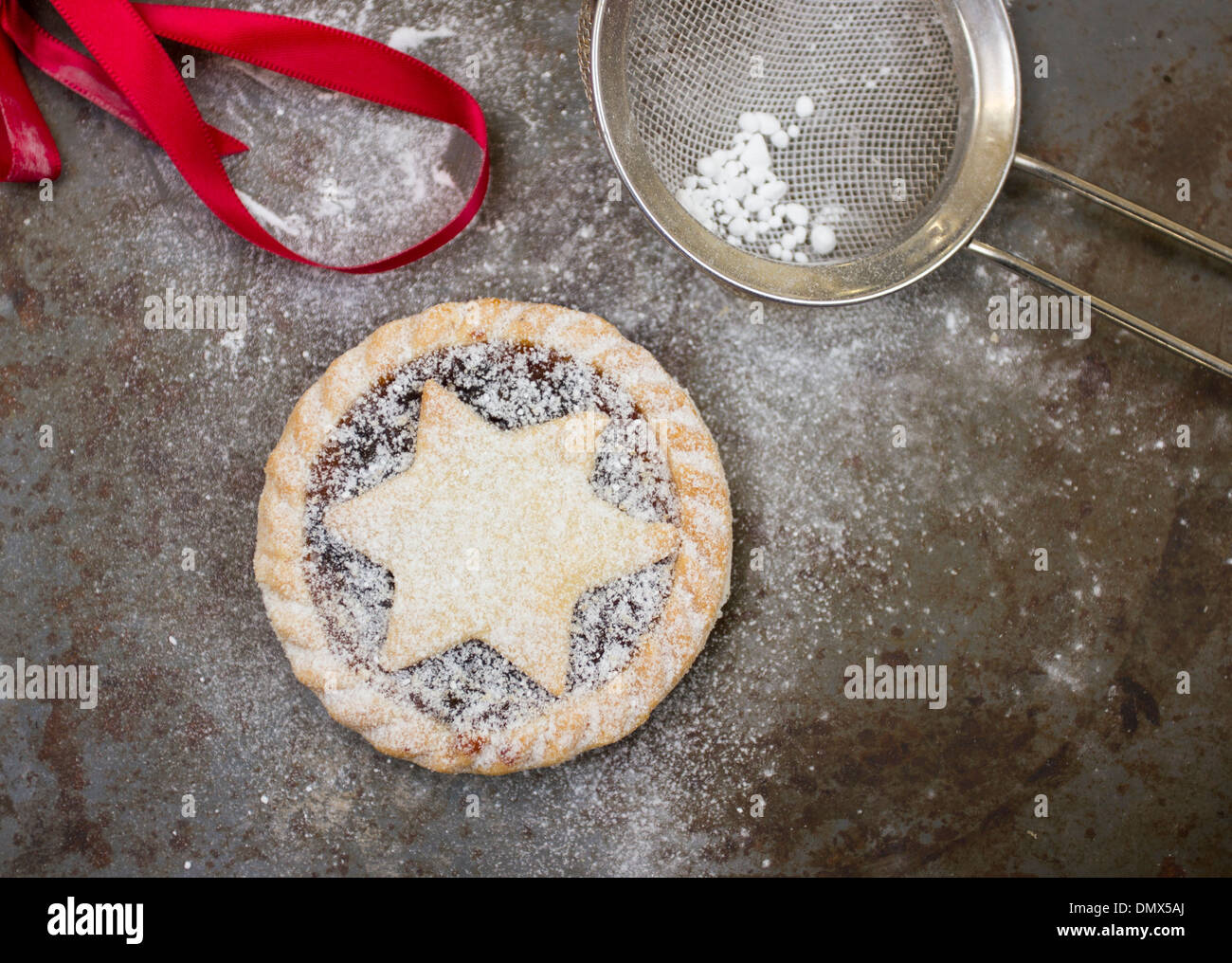 Home made icing sugar dusted mince pie with red ribbon and sieve on ...