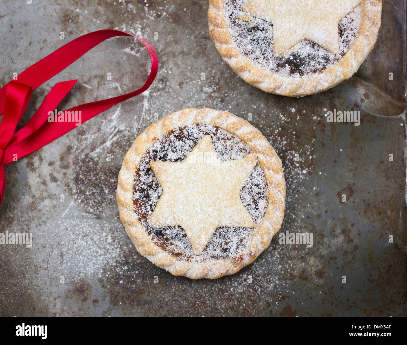 Home made icing sugar dusted mince pies on grey rustic surface with red ...