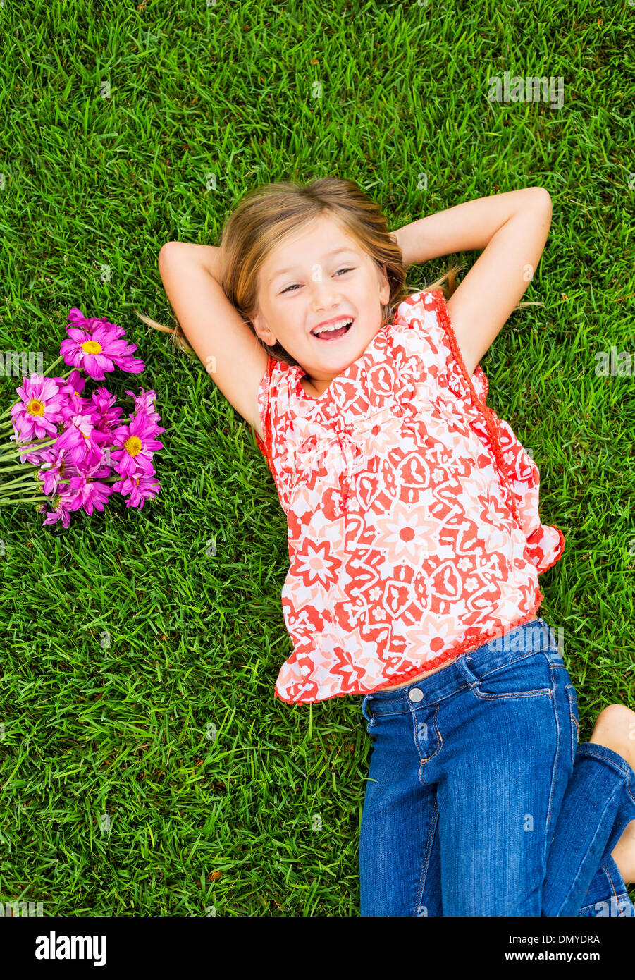 Smiling cute little girl lying on green grass relaxing with flowers ...