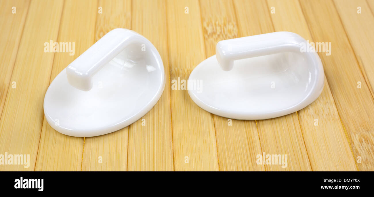 Two new plastic stick on mounting hooks atop a wood slat background ...