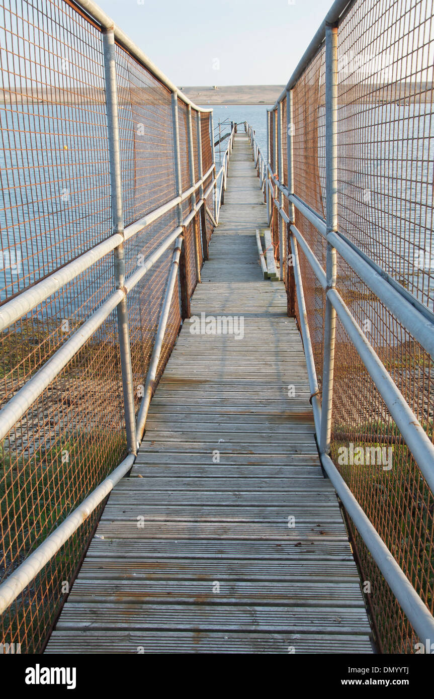 English seashore. A rickety old wooden jetty projects into the brackish ...