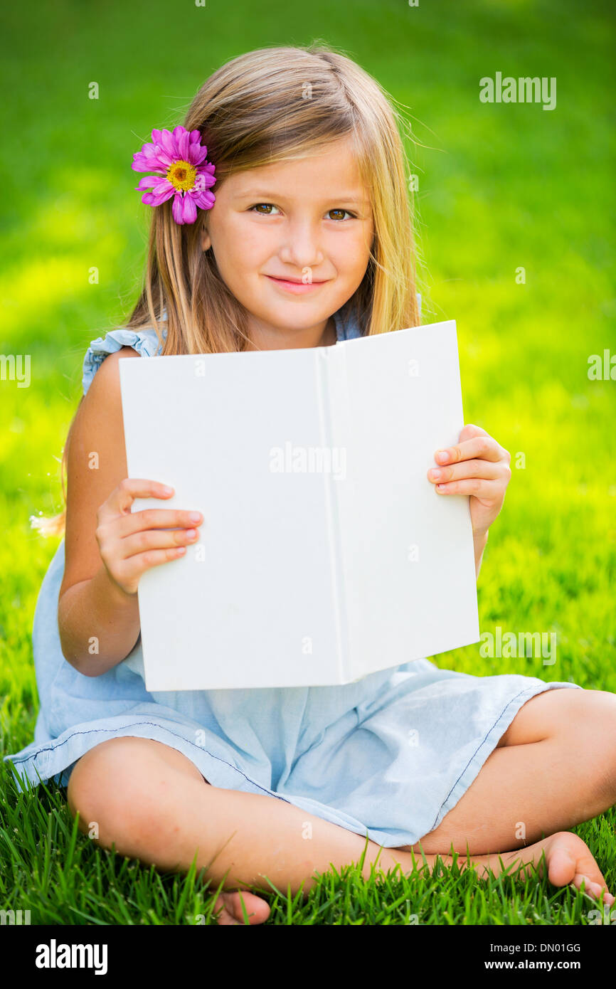 Cute little girl reading book outside on grass in backyard Stock Photo ...