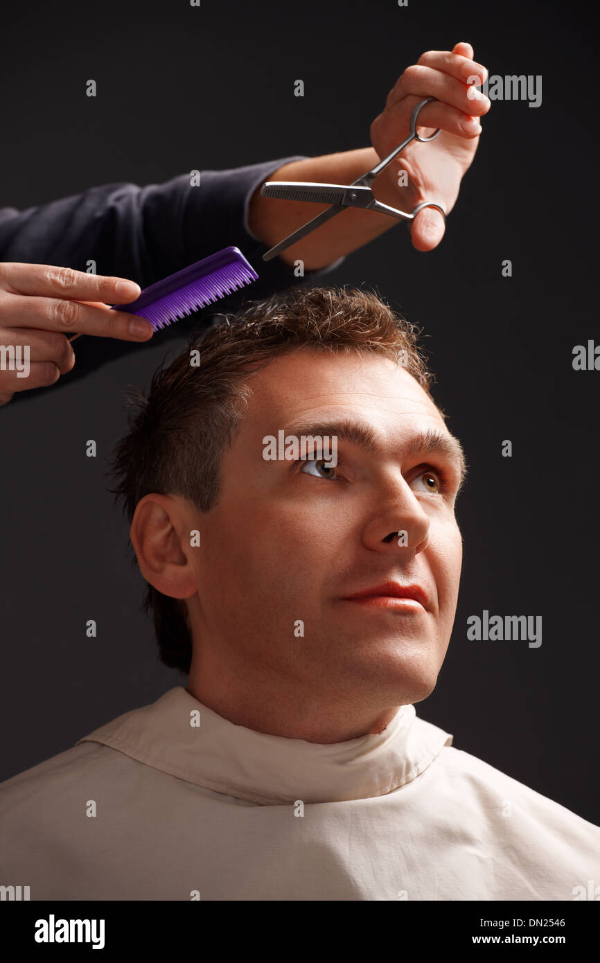 Barber cutting hair with scissors and comb, a client is a young ...