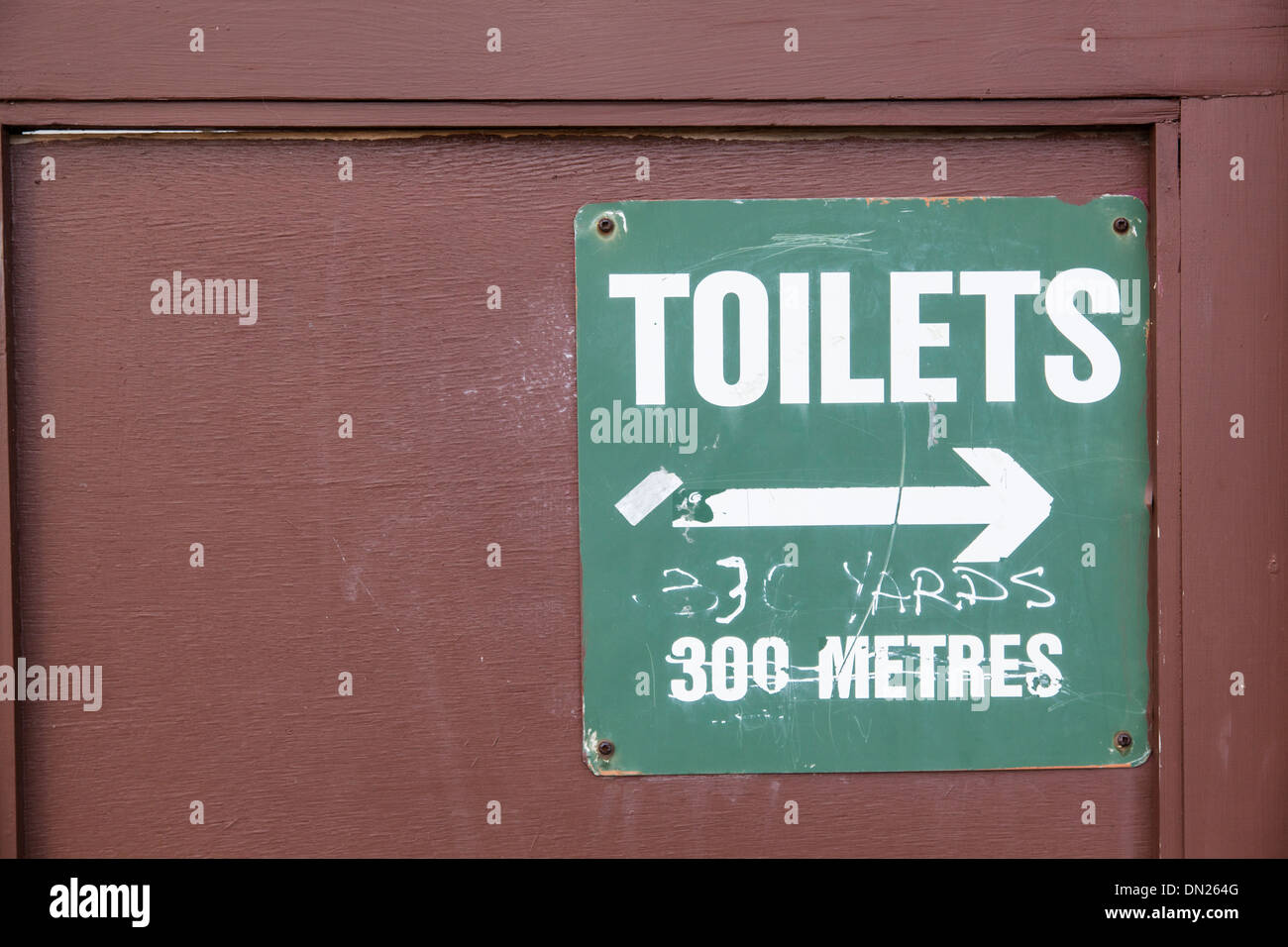 Sign for public toilets on wall giving distance in meters crossed out ...