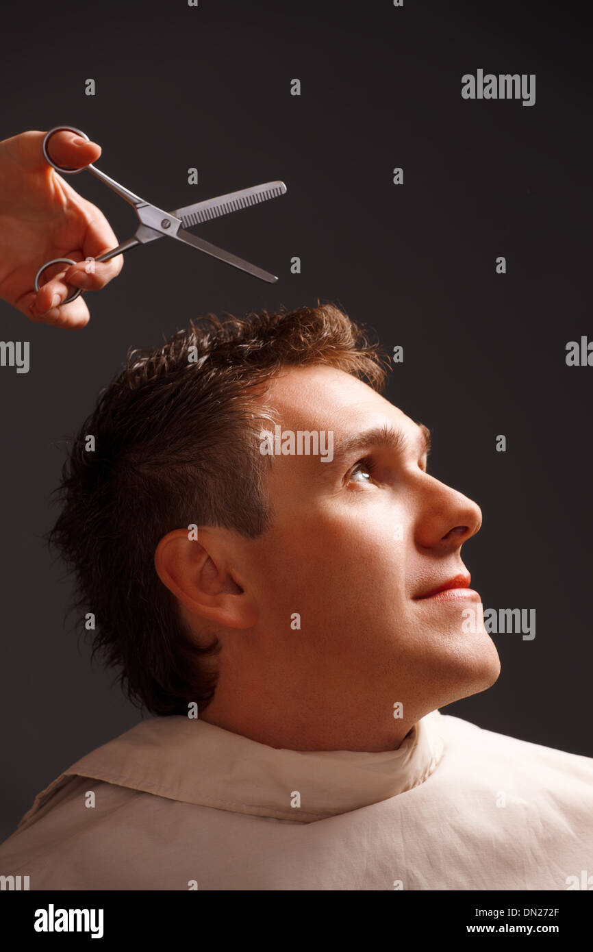 Barber cutting hair with scissors, a client is a young caucasian man ...