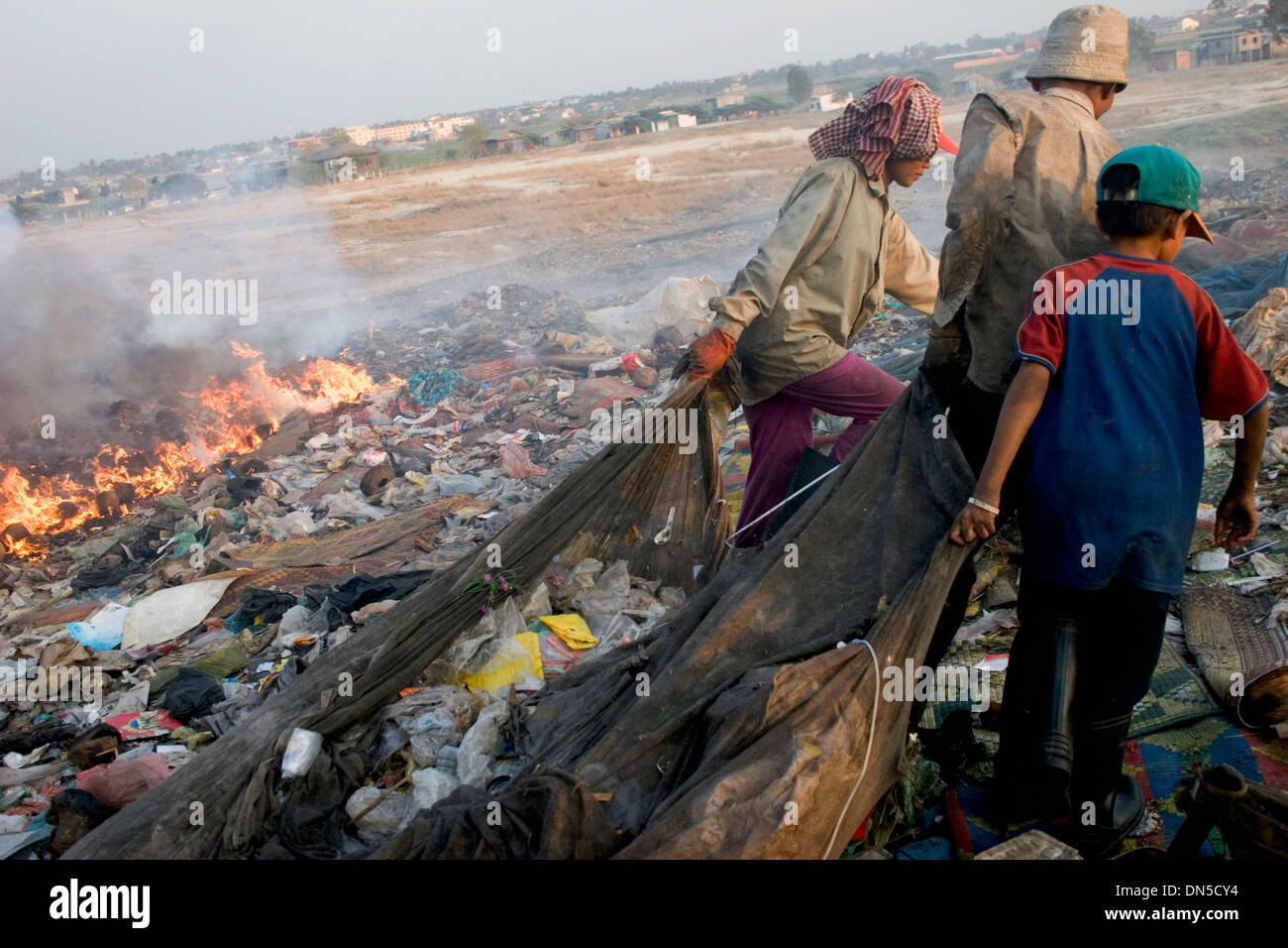 Workers are working near flaming piles of garbage at the polluted and ...