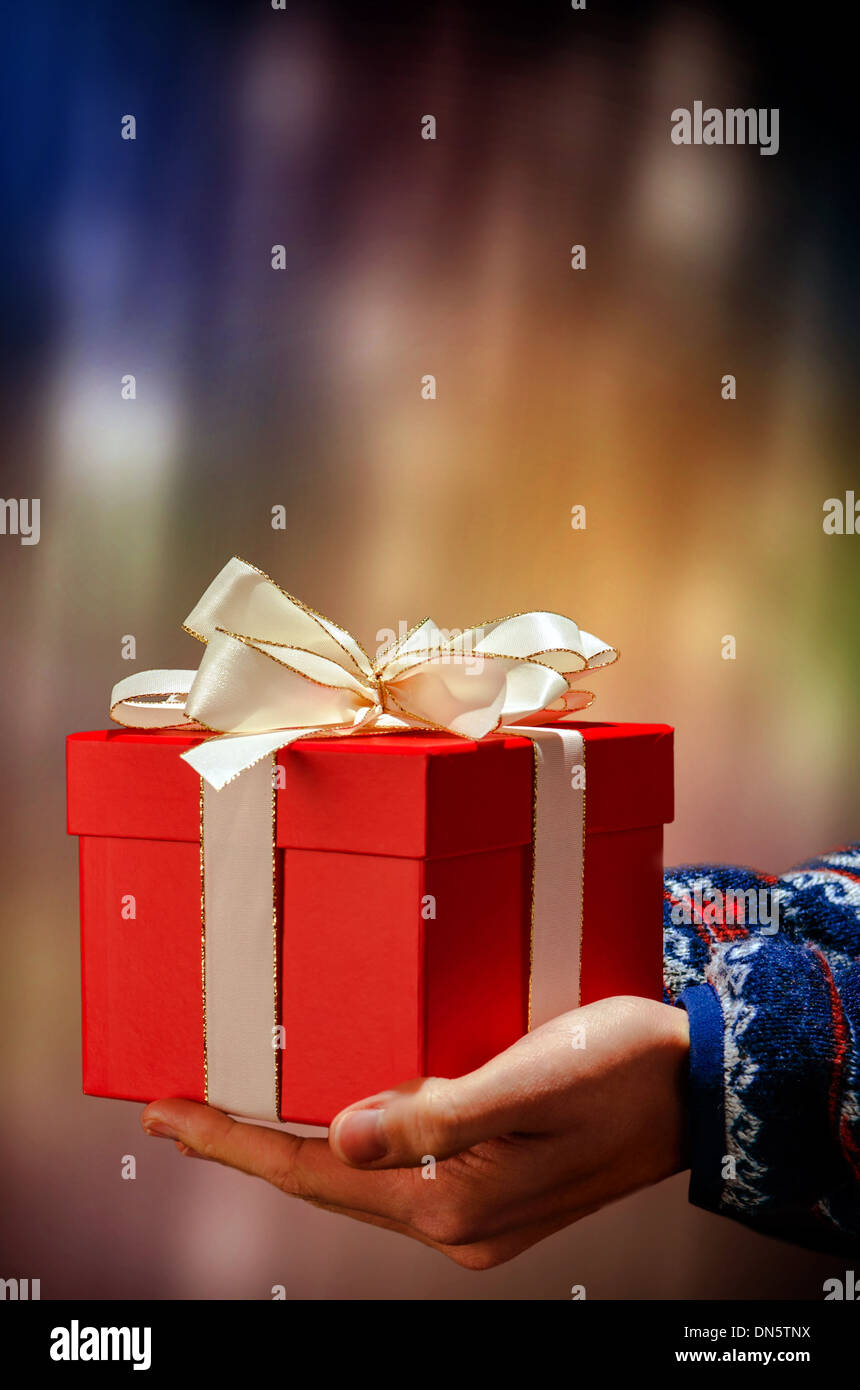 two hands hold a red present with white ribbon before coloured ...