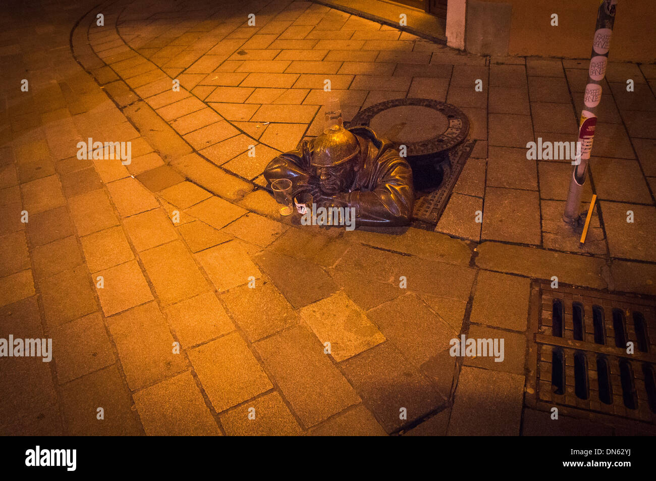 bronze statue of a man playfully peeking out from under a manhole cover ...