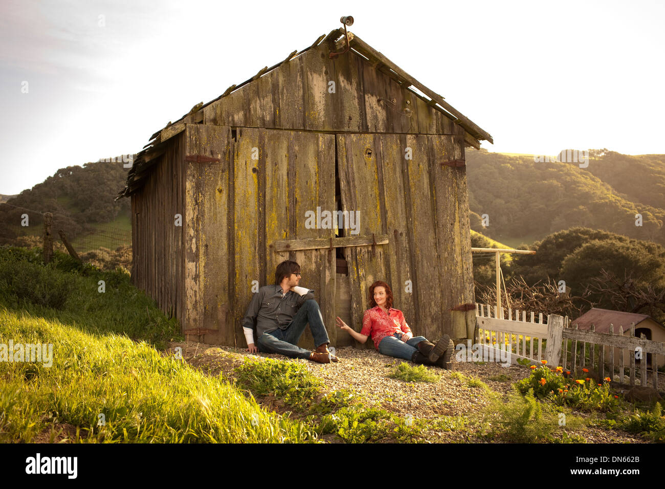 Couple sitting against barn in rural landscape Stock Photo - Alamy