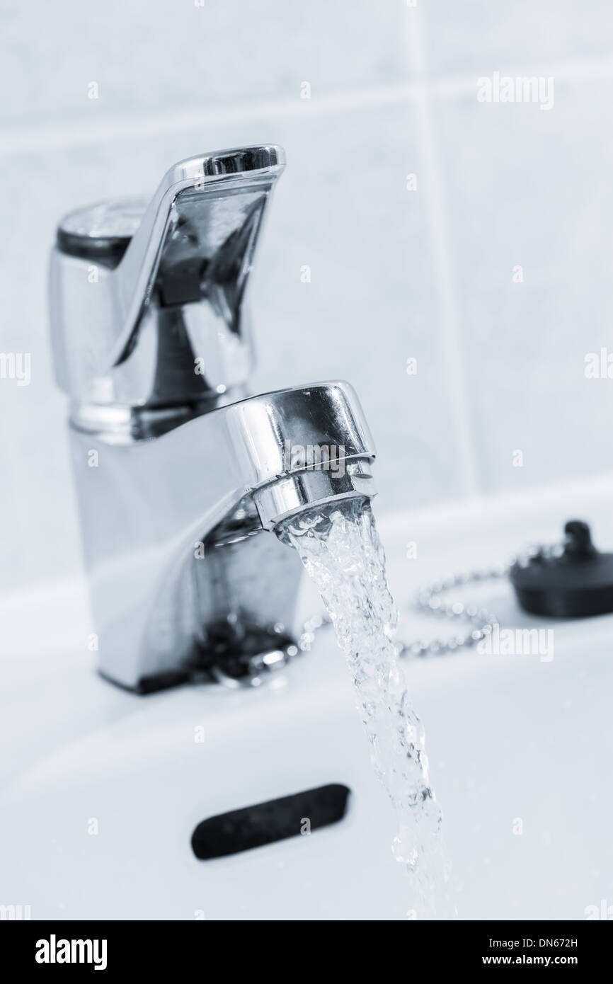 Open faucet in bathroom, water is running, tinted black and white image ...