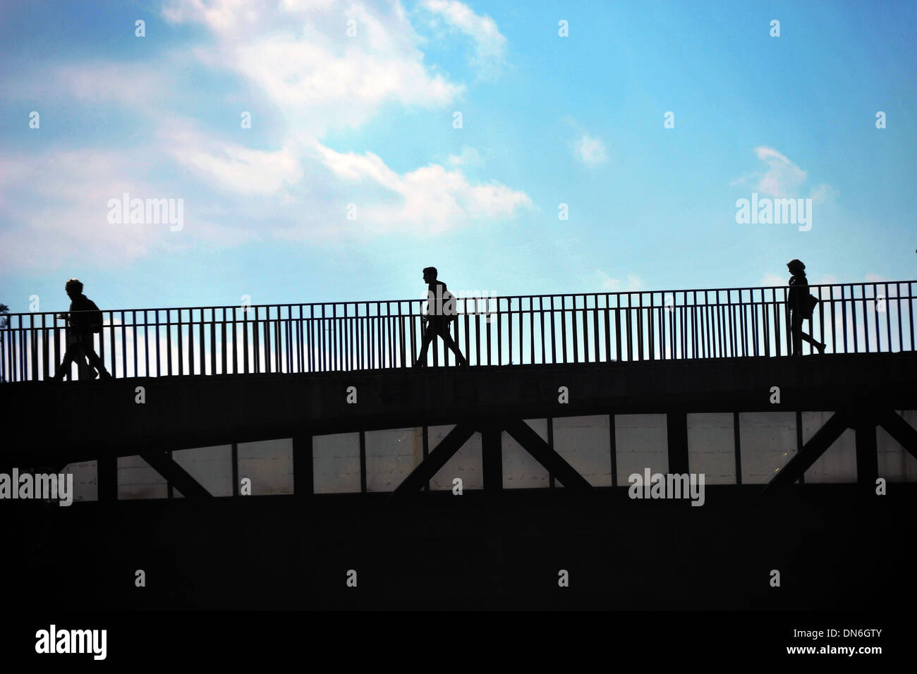 The silhouettes of three pedestrians crossing a footpath over a ...