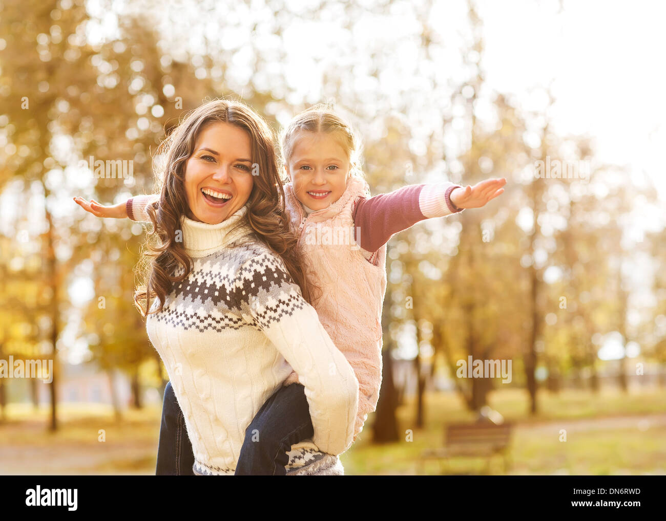 Mother giving daughter piggyback ride in autumn woodland Stock Photo ...