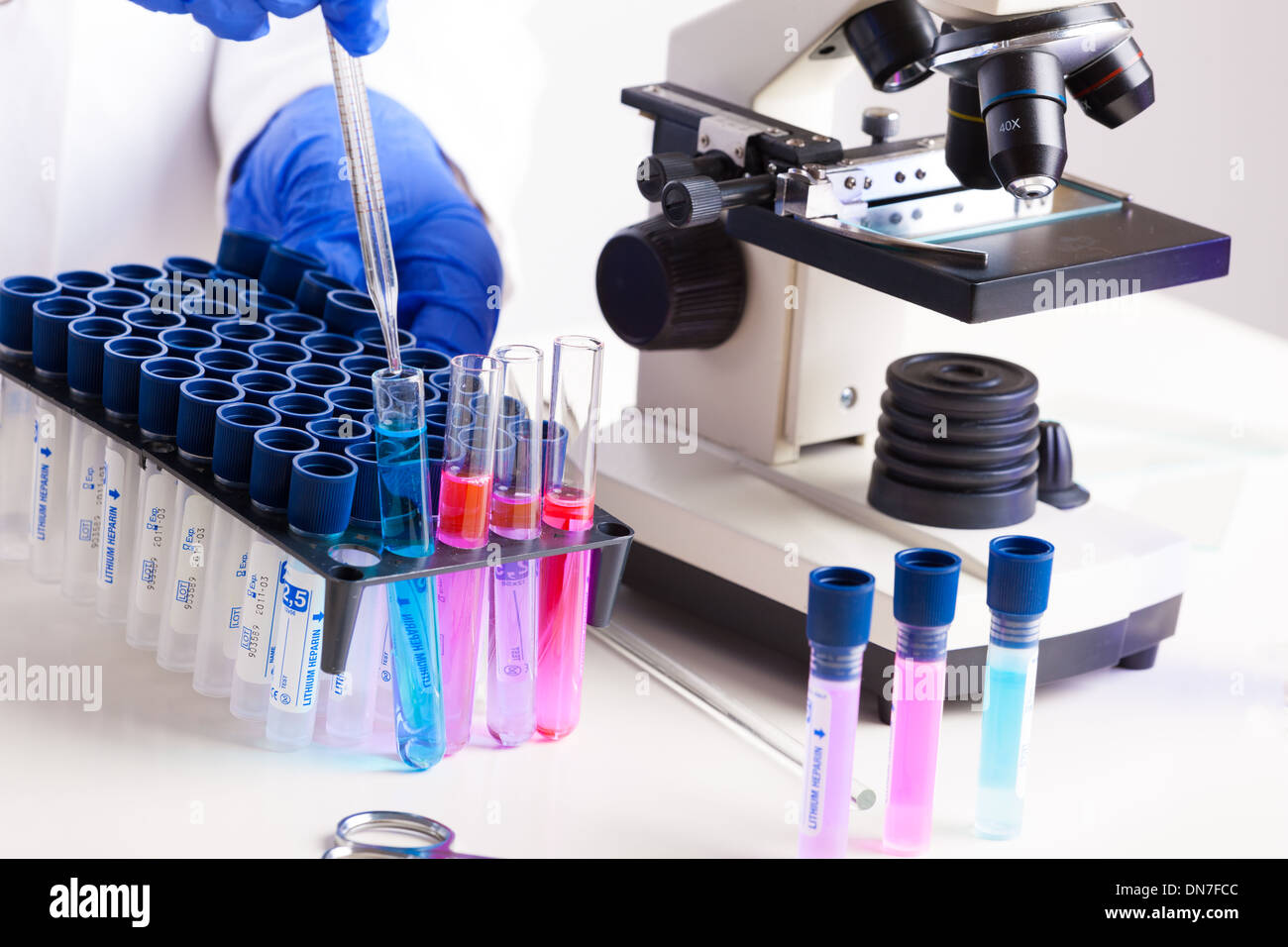 Lab technician working with equipment: tweezers, microscope, test tubes ...