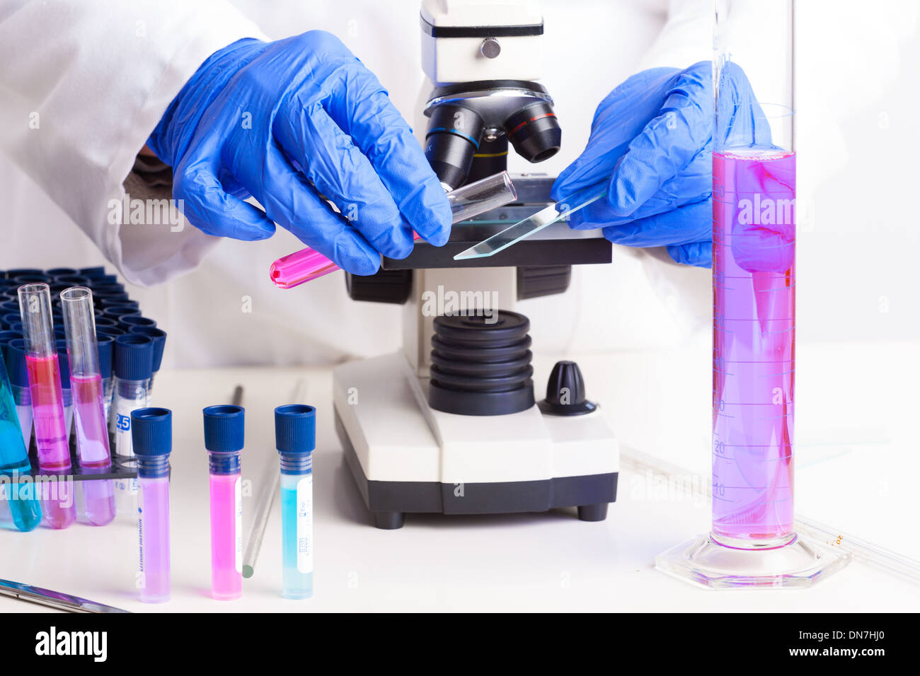 Lab technician working with equipment: tweezers, microscope, test tubes ...